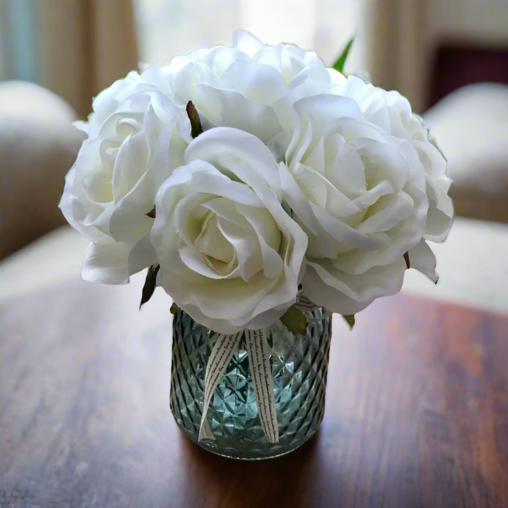 A flower arrangement of ivory artificial roses in blue cut glass vase ...